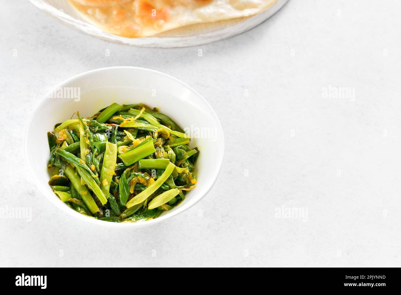 Indian style spring onion stir fry in bowl over white background with ...
