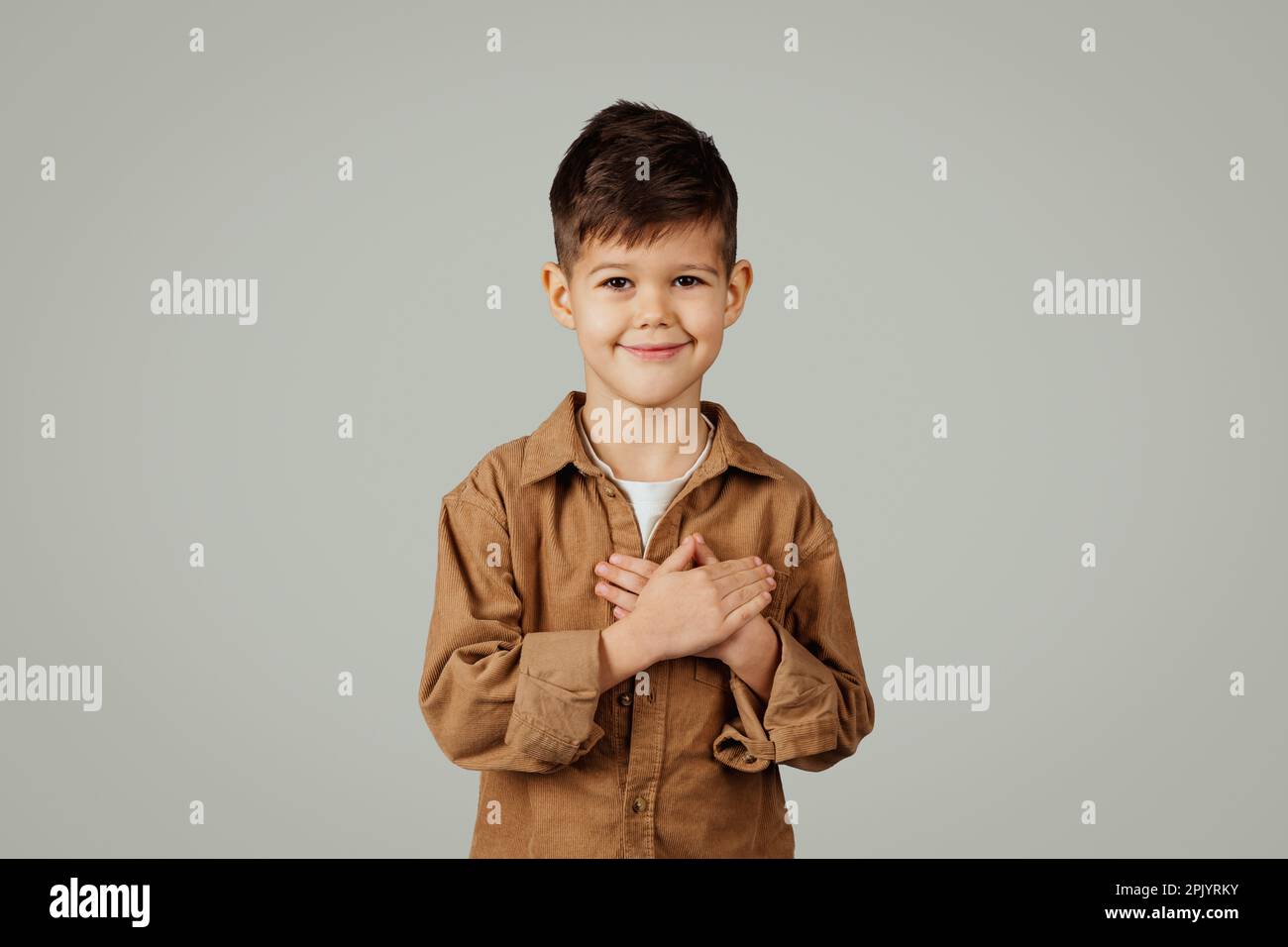 Cheerful caucasian 6 years old little boy in casual presses hands to ...