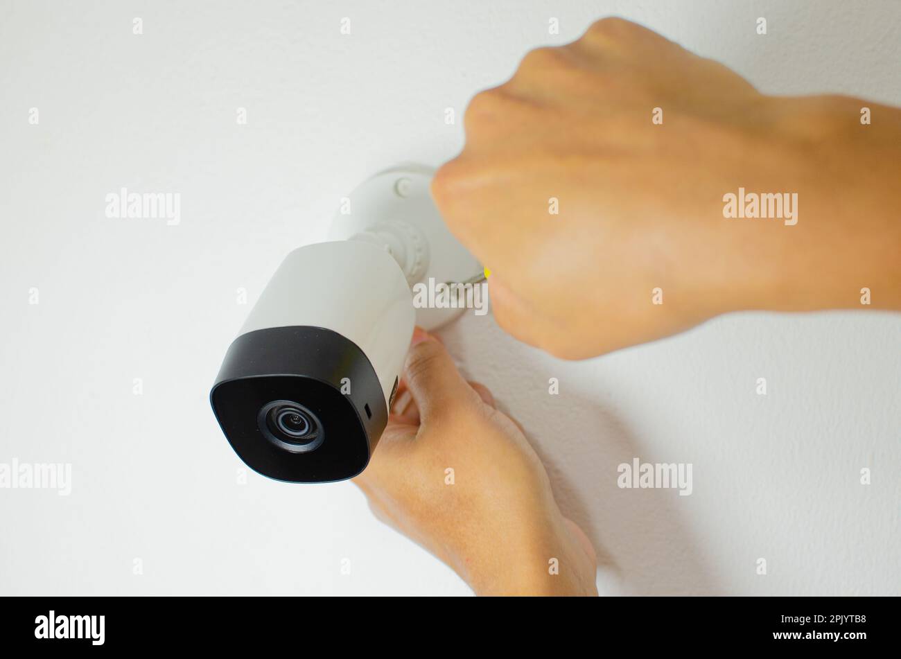 A closeup of hands installing a home security camera on a white wall ...
