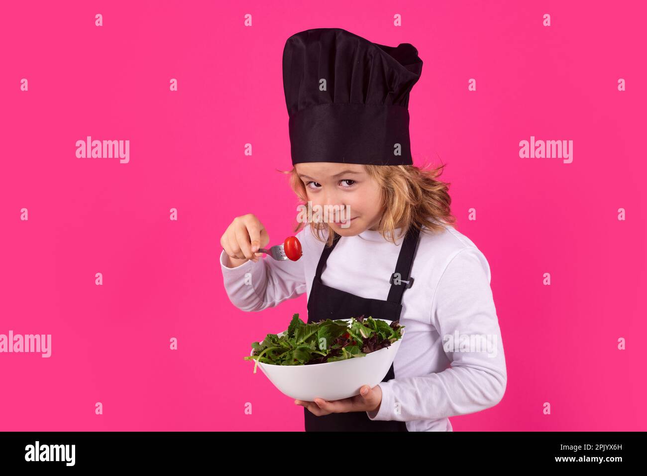 Kid cook hold plate with vegetables and fork with tomato. Excited chef ...