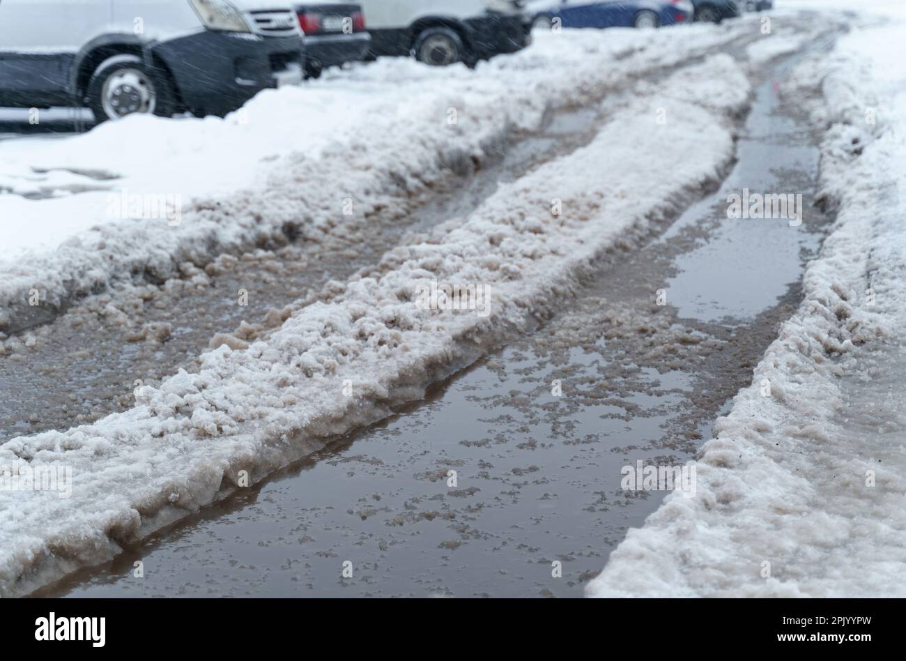 The road is covered with snow and slush, cars are parked on the side of ...