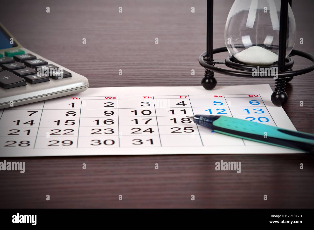 business calendar page on table, sandglass, calculator and pen, close ...