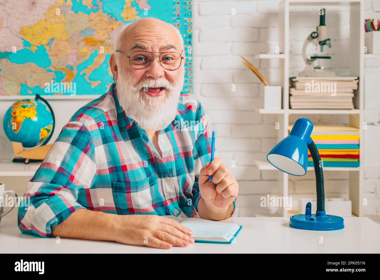 Happy mature teacher sitting in classroom. Cheerful teacher who loves ...