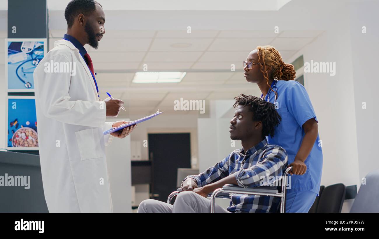 Doctor consulting wheelchair user with physical disability, meeting in ...