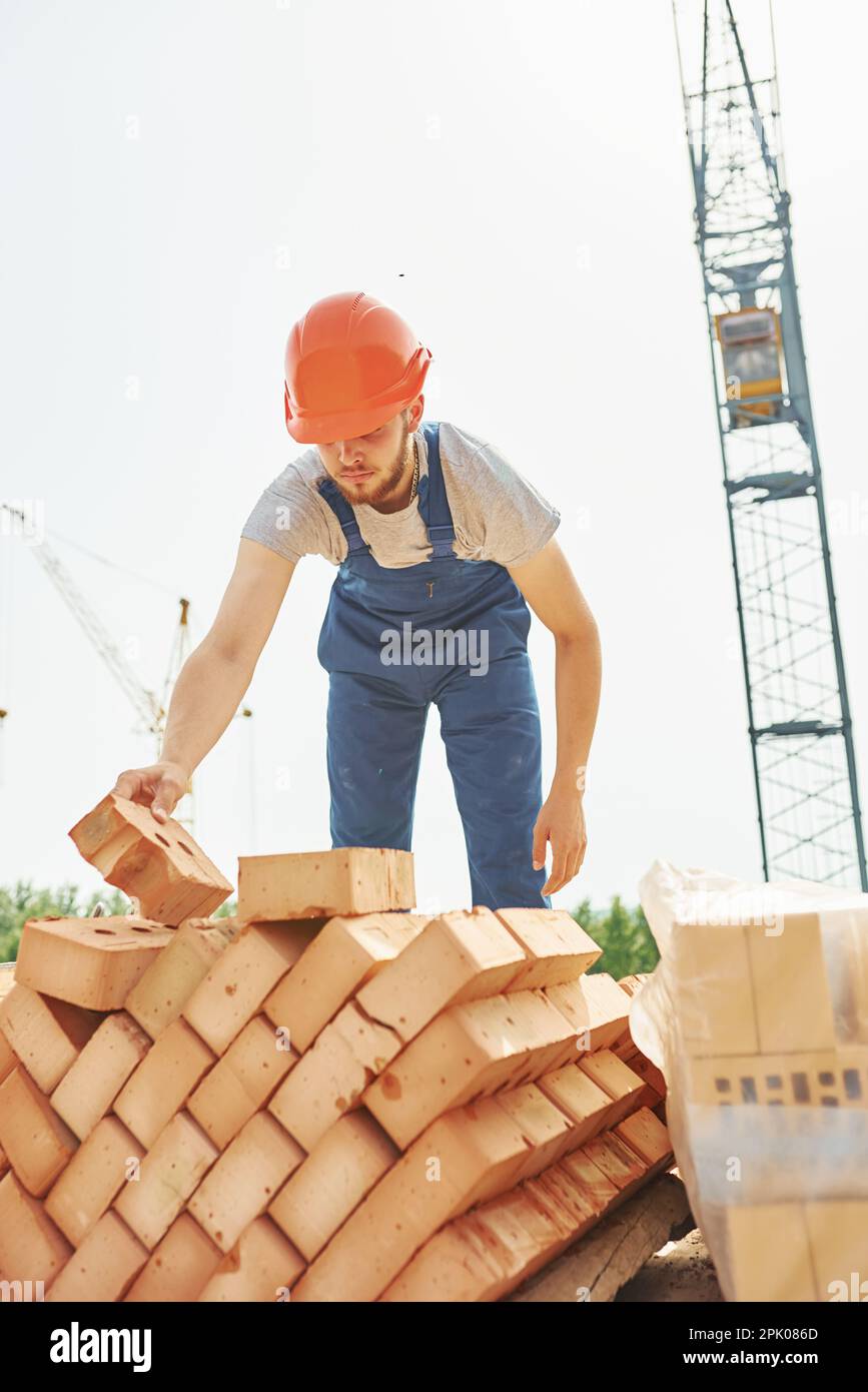 Holding bricks. Young construction worker in uniform is busy at the ...