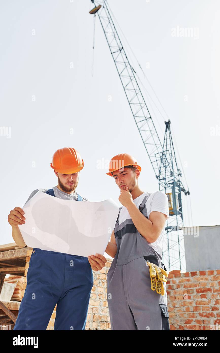 Reading plan. Two young construction workers in uniforms is busy at the ...