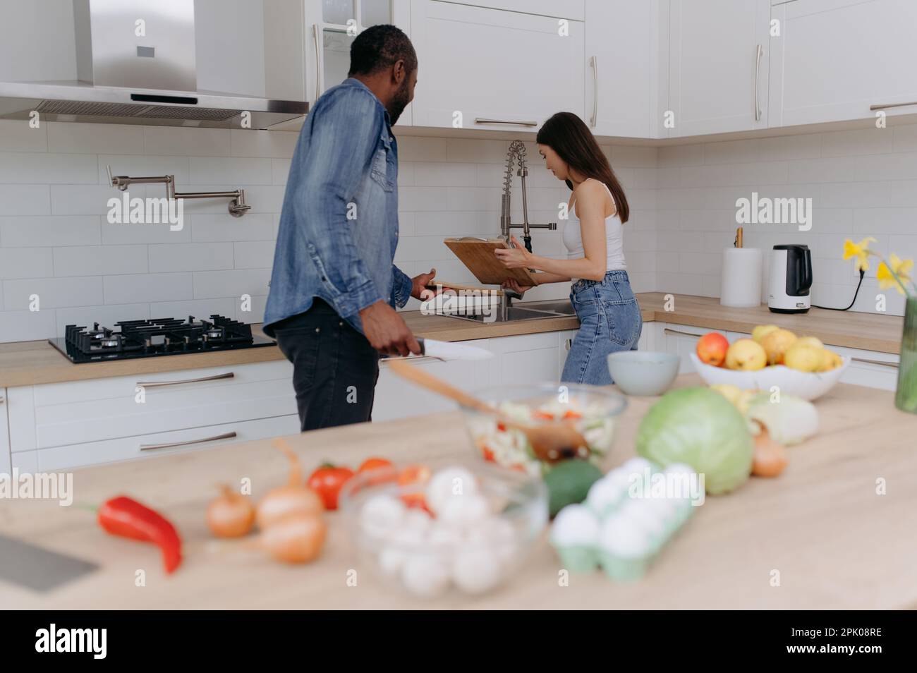 A happy young couple is busy in the kitchen. A black man and a young ...