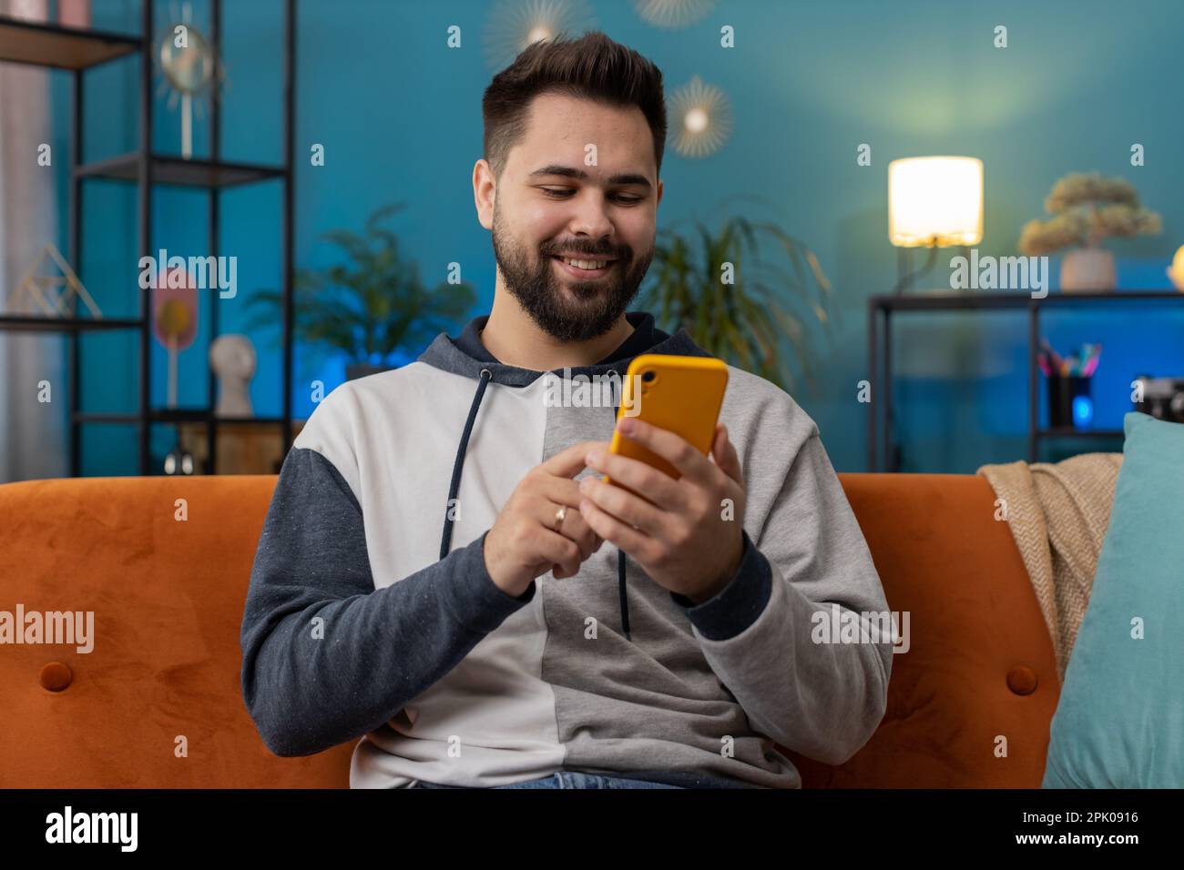 Caucasian man sitting on couch uses mobile phone smiles at home living ...