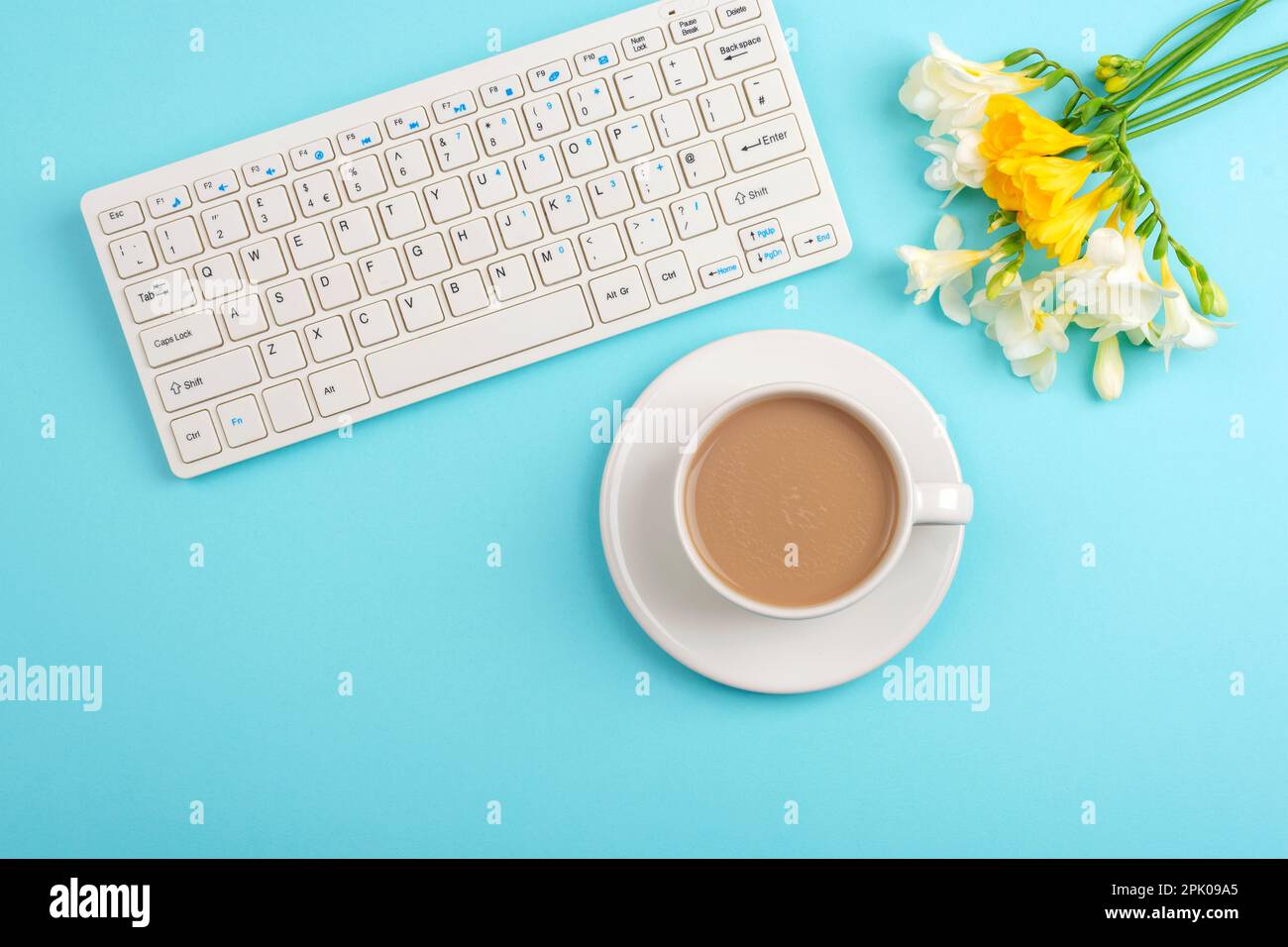 Computer keyboard and coffee cup on turquoise table with freesia ...