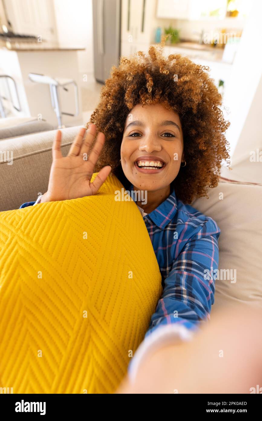 Portrait of happy biracial young woman with afro hair waving hand while ...