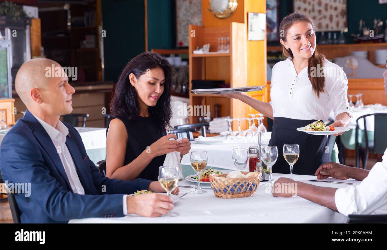 Smiling waitress serving meals to guests in restaurant Stock Photo - Alamy