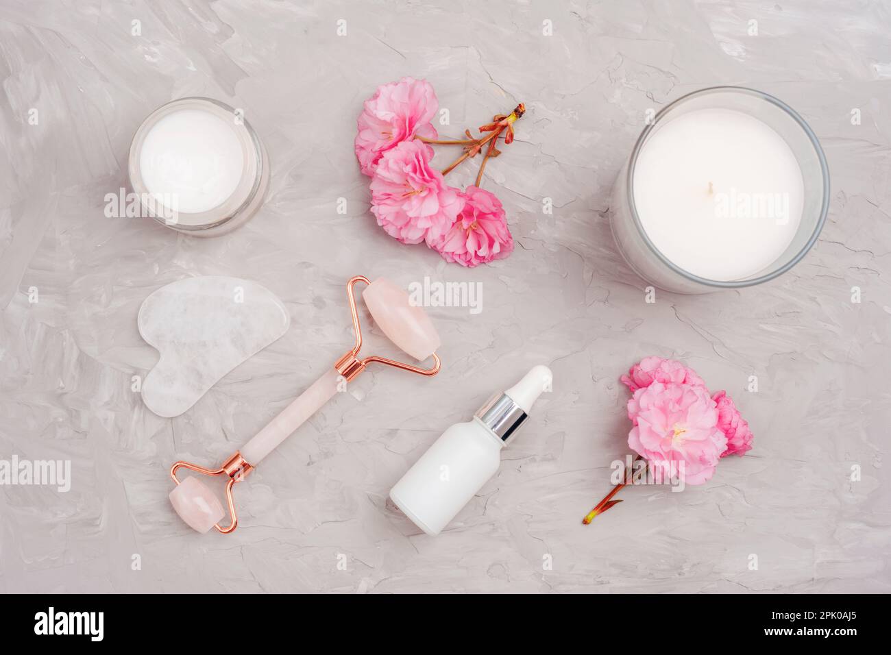 Cream jar, face roller, gua sha stone and pink cherry blossom on gray ...