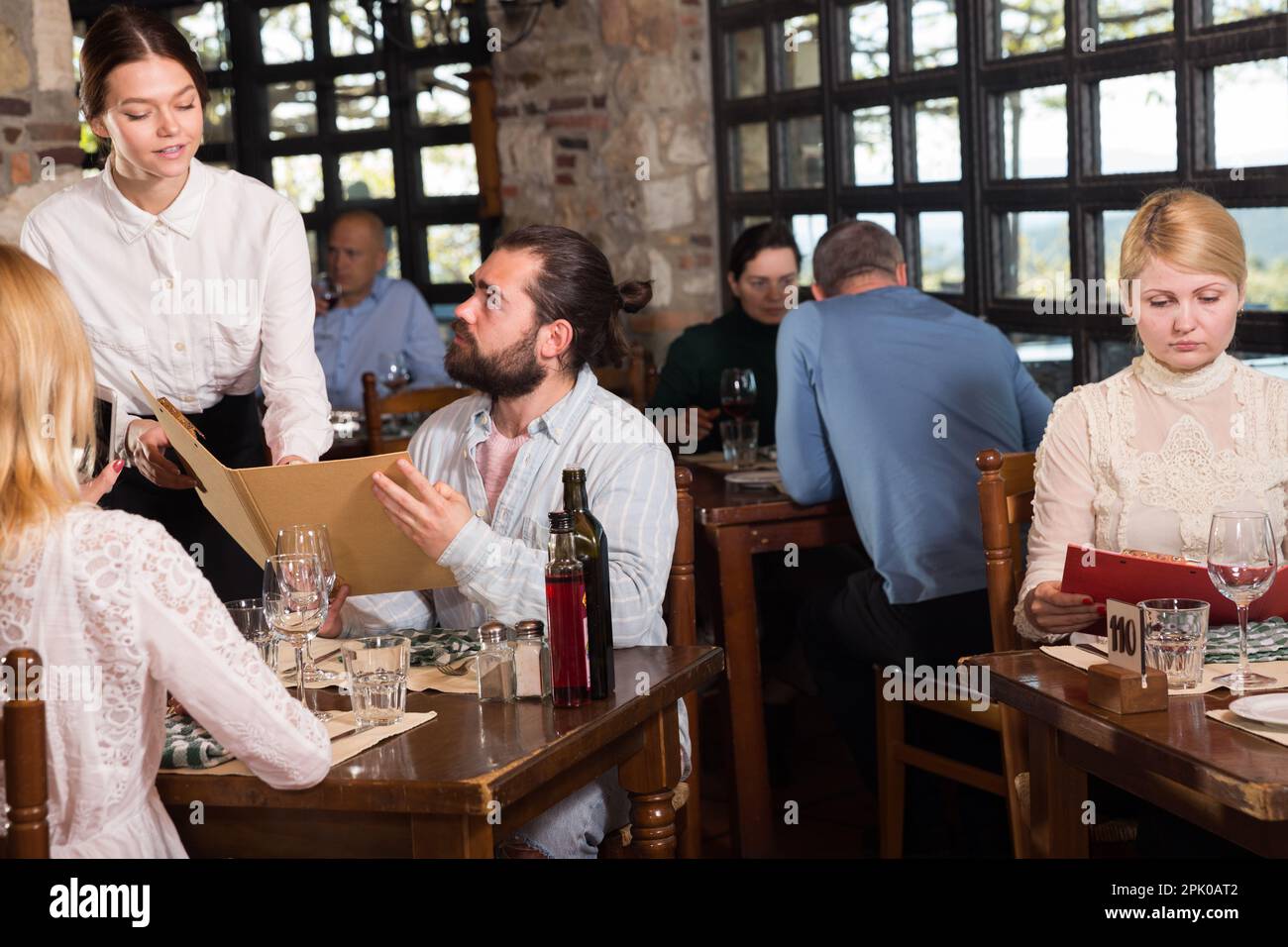 Charming young waiter receiving order from guests in country restaurant ...