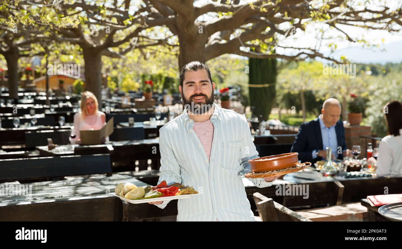 Adult beard waiter who is standing with order at country outdoor ...