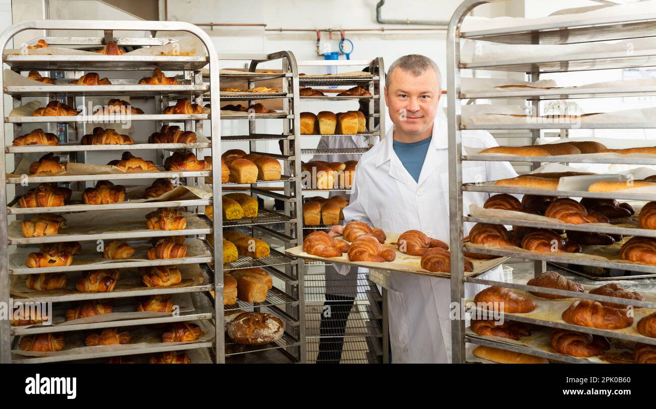 Baker putting baked bread on rack Stock Photo - Alamy