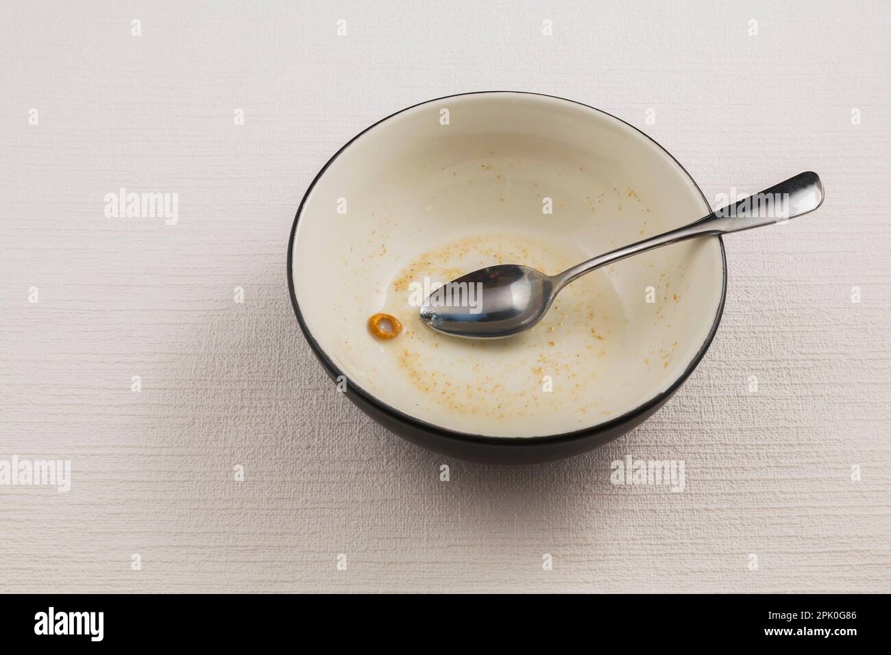 Almost empty bowl of cereal with spoon on white textured background ...
