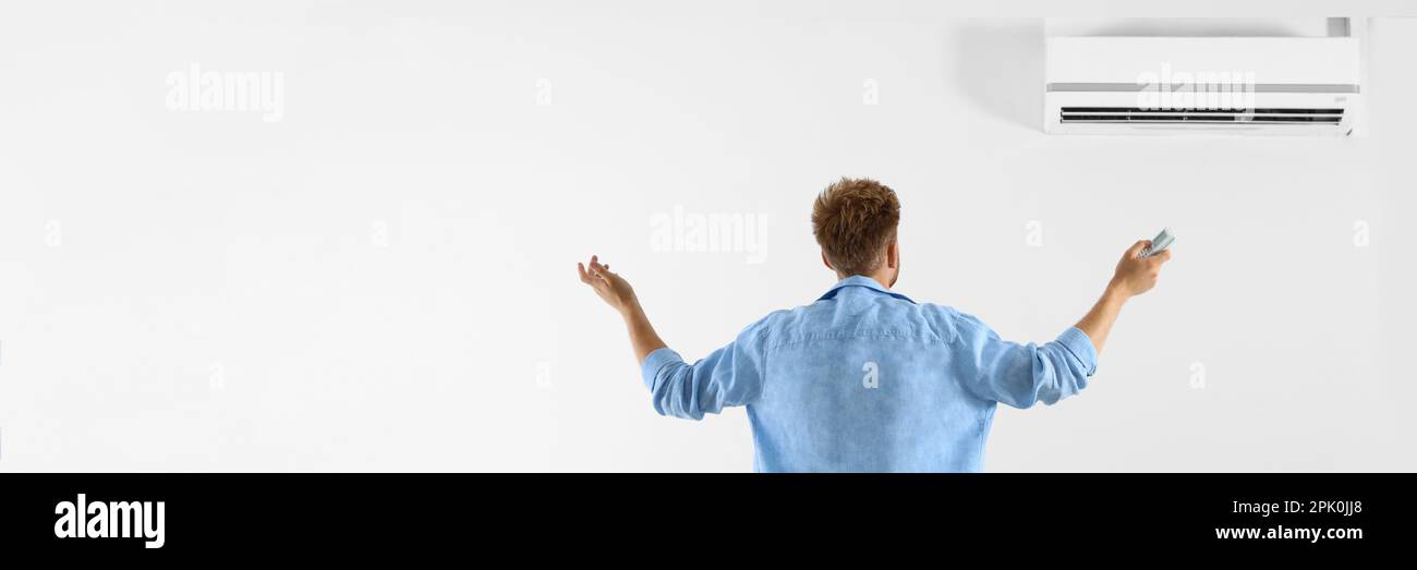 Young man operating air conditioner with remote control indoors, space ...