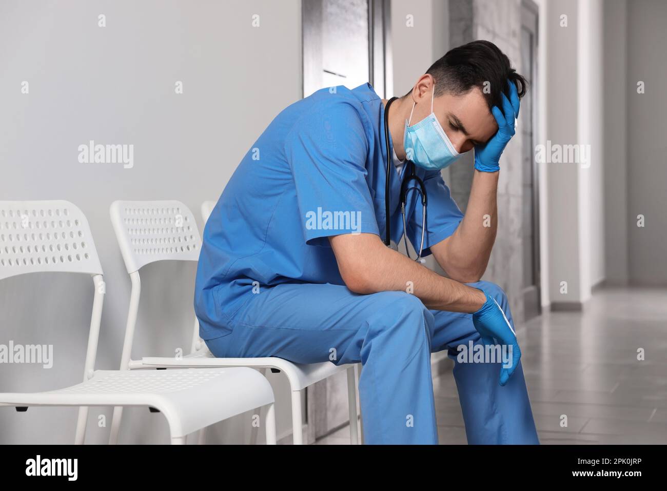 Exhausted doctor sitting on chair in hospital hallway Stock Photo - Alamy