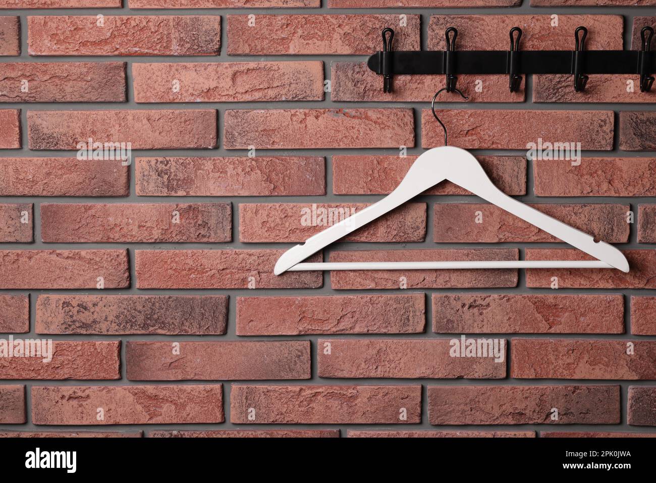 Hook rack with white clothes hanger on red brick wall. Space for text ...