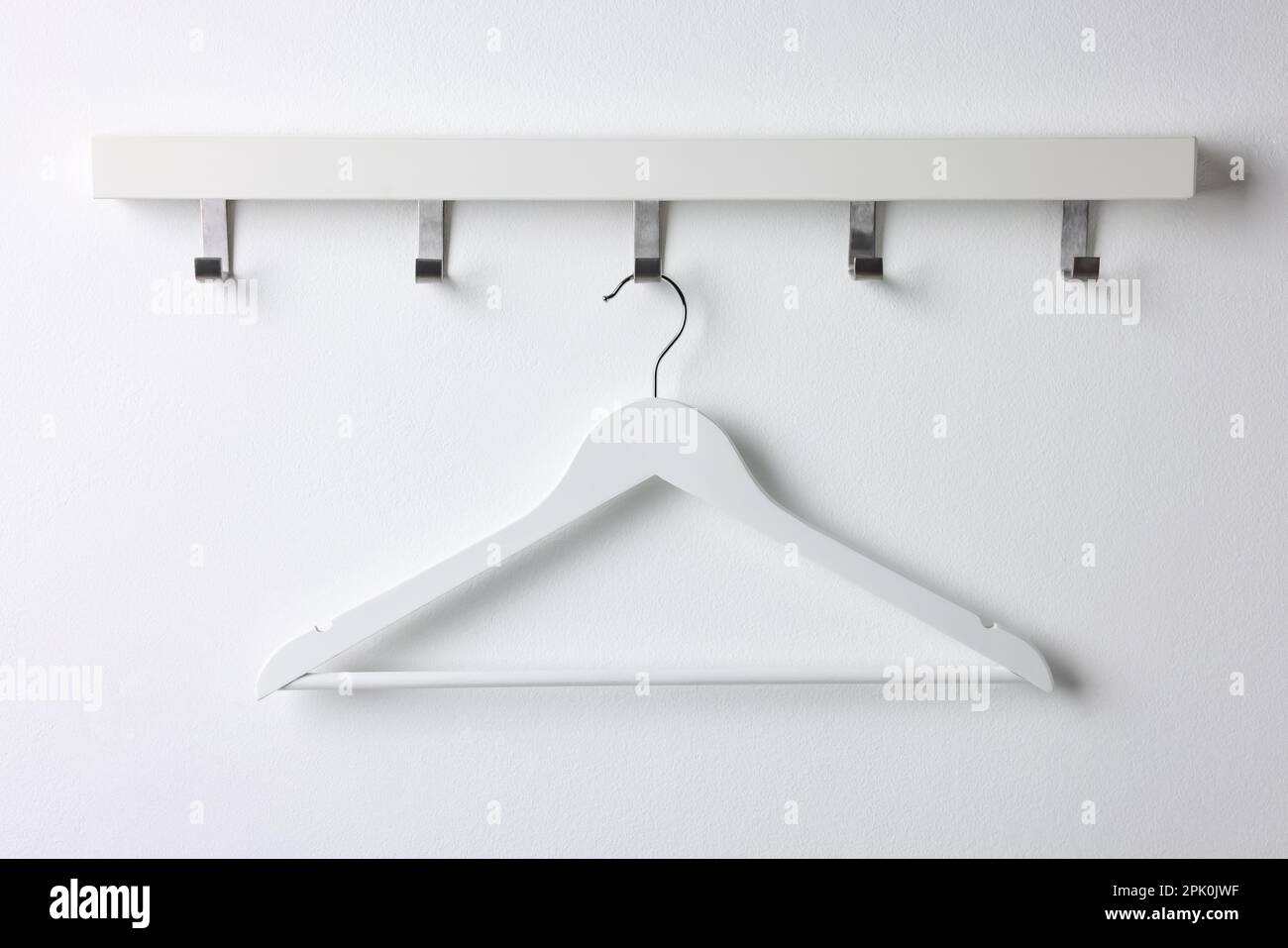 Rack with empty clothes hanger on white wall Stock Photo - Alamy