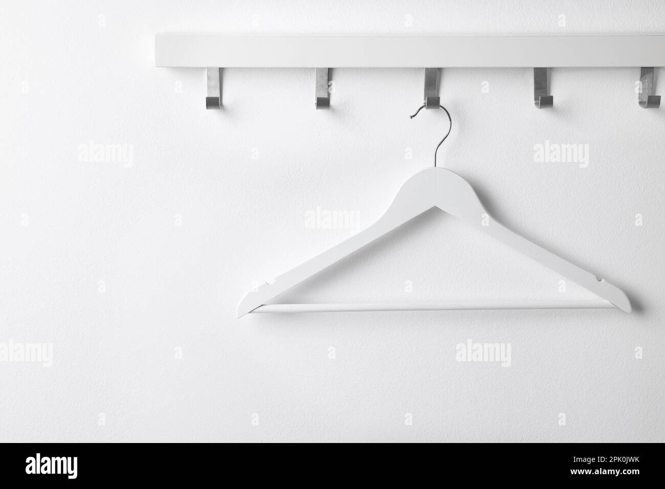 Rack with empty clothes hanger on white wall Stock Photo - Alamy