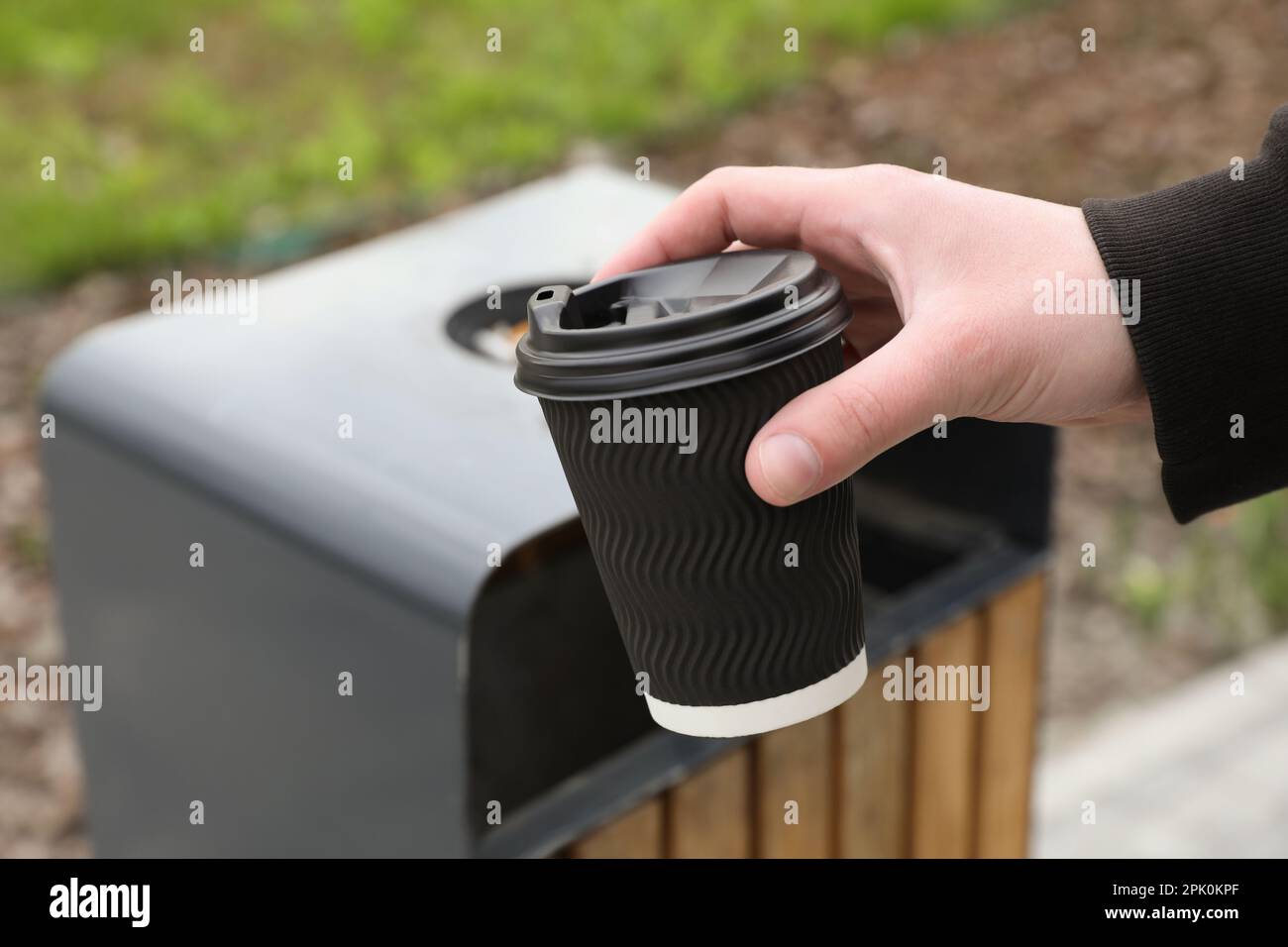Man throwing black paper cup into trash can outdoors, closeup. Space ...