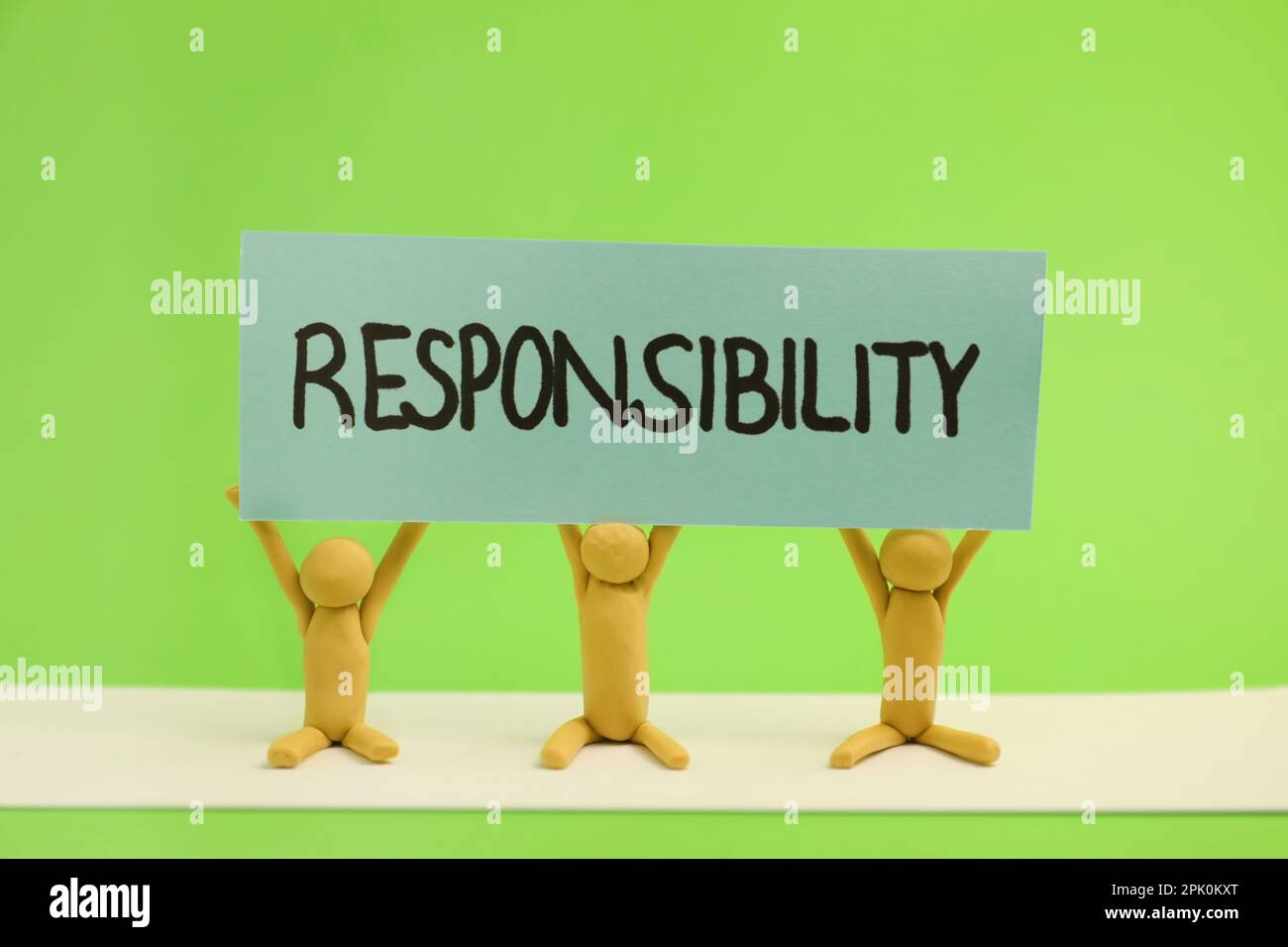 Three plasticine human figures holding card with word Responsibility on green background Stock ...