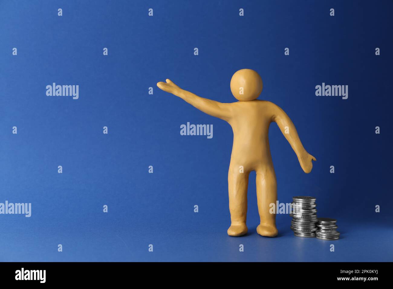 Human figure made of yellow plasticine with stacked coins on blue ...