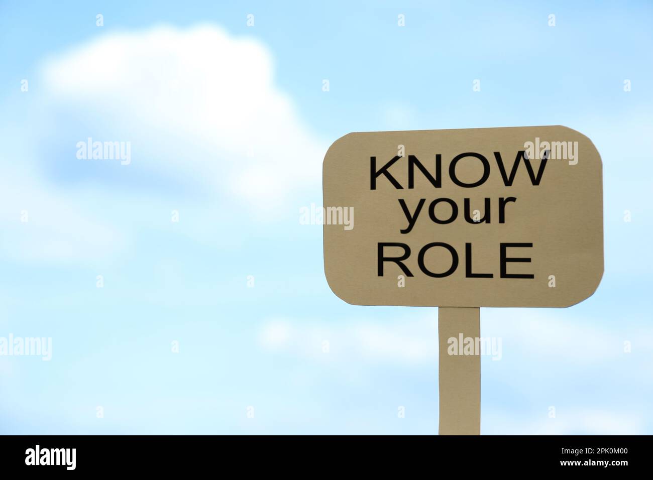 Cardboard sign with phrase Know Your Role against cloudy sky, space for ...