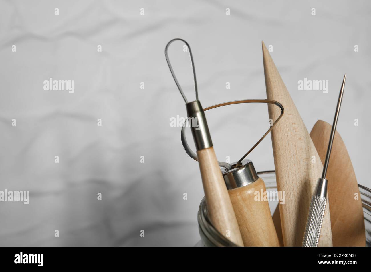 Set of clay modeling tools in glass jar near white wall, closeup. Space ...