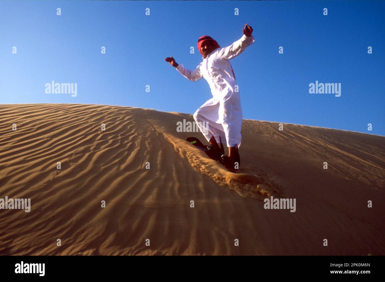 Arab man sand surfing on a skateboard down a dune in Dubai, UAE Stock ...