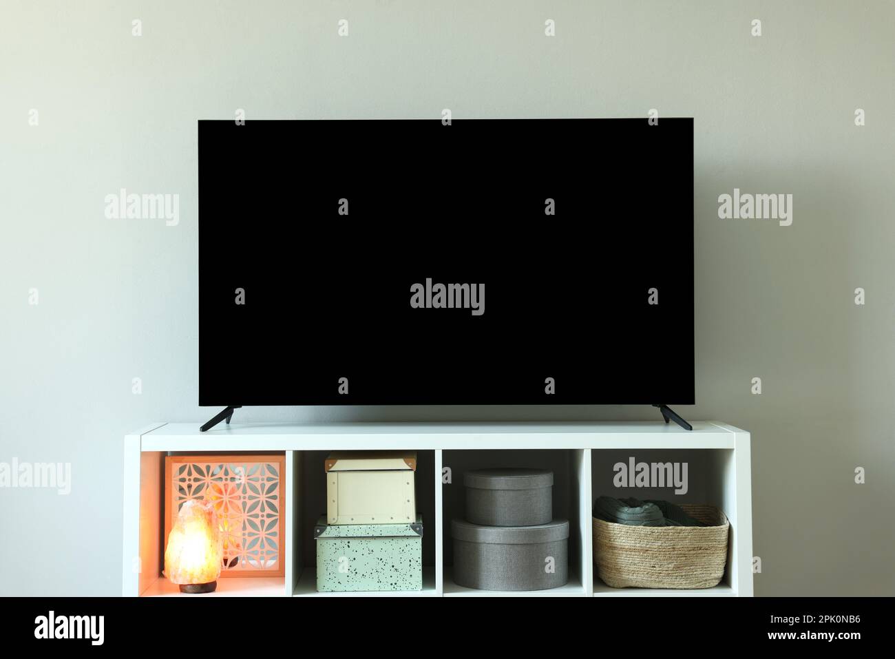 Modern TV and lamp on cabinet near white wall indoors. Interior design ...