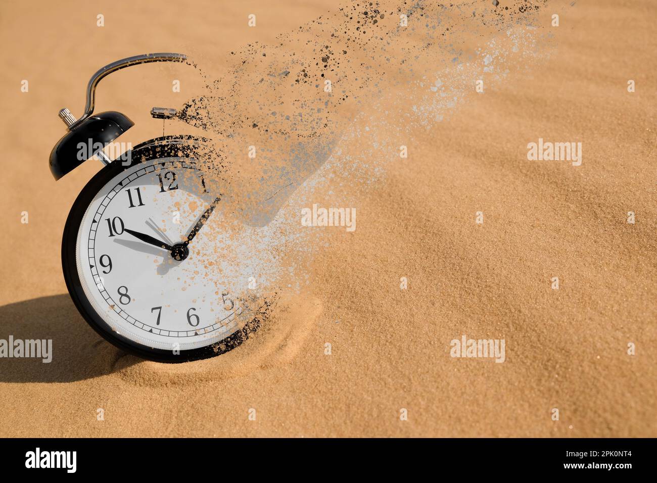 Time is running out. Black alarm clock vanishing on sand in desert ...
