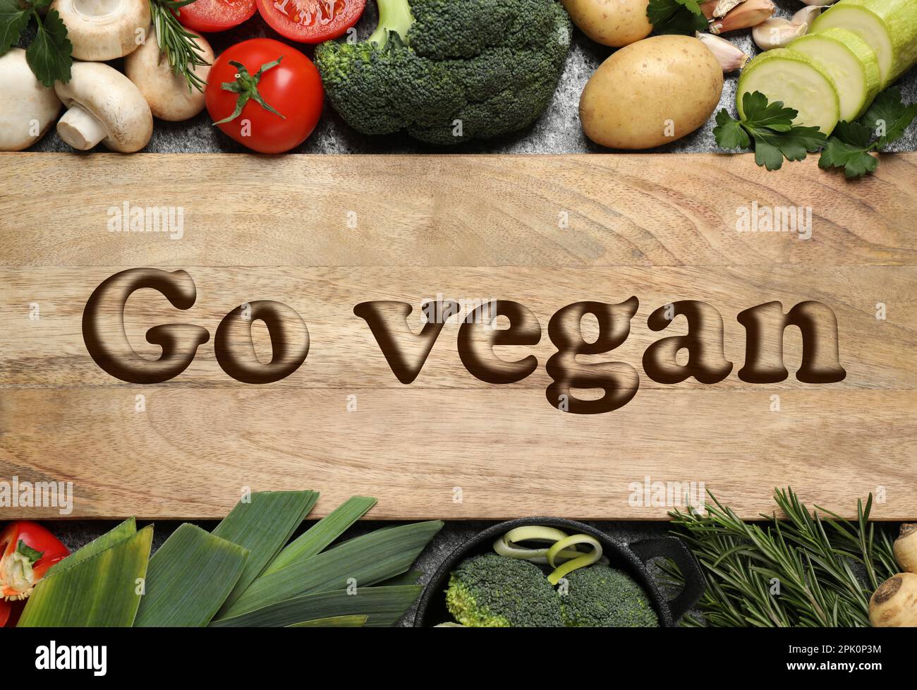 Wooden board with phrase Go Vegan and fresh vegetables on table, flat ...