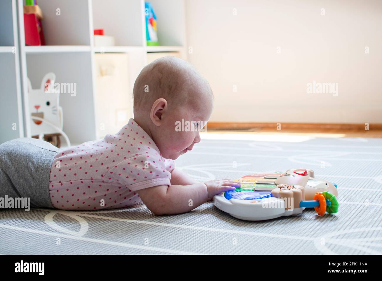 Little caucasian newborn baby girl playing with a piano toy on the ...