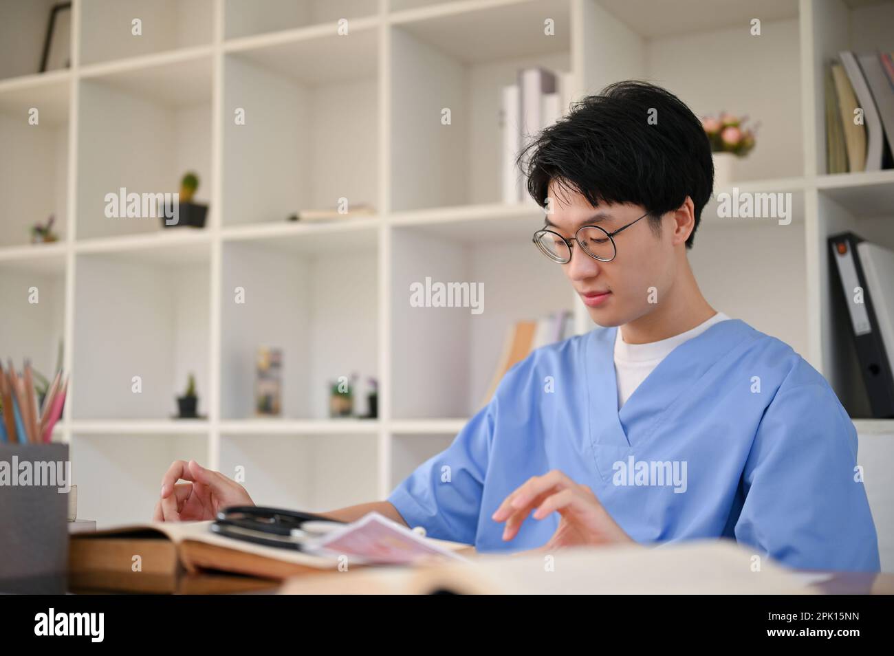 Smart young Asian male medical student in a uniform focuses on reading ...