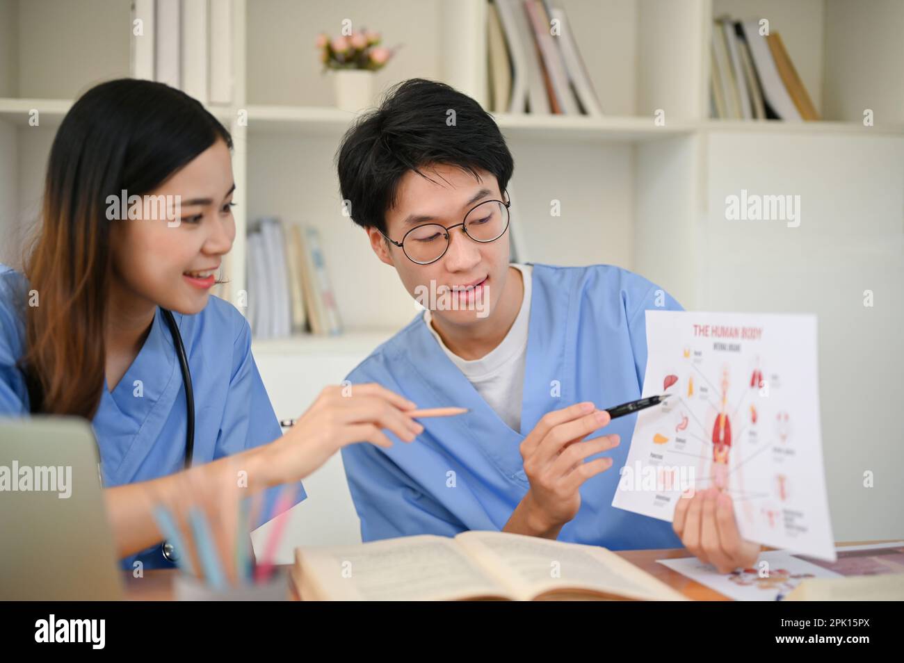 Smart young Asian male medical student is explaining and tutoring the ...