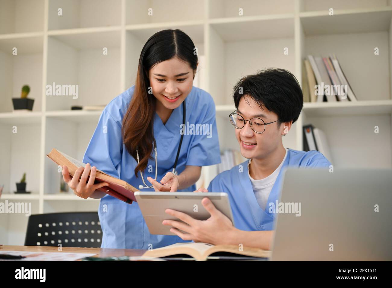 Two smart young Asian medical students are talking, using tablet and ...