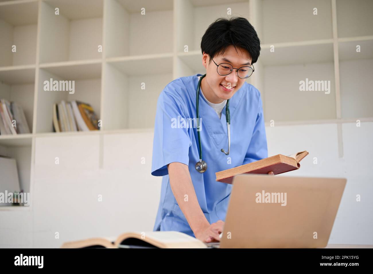 Smart young Asian male medical student leaning on table, using laptop ...