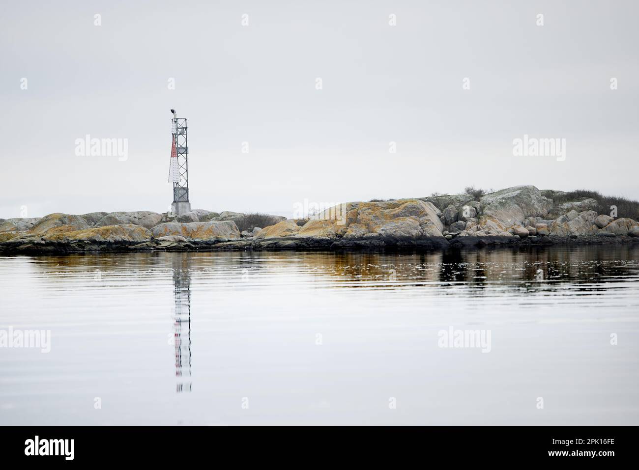A small light house on a scaur by the coast line with its reflection in ...
