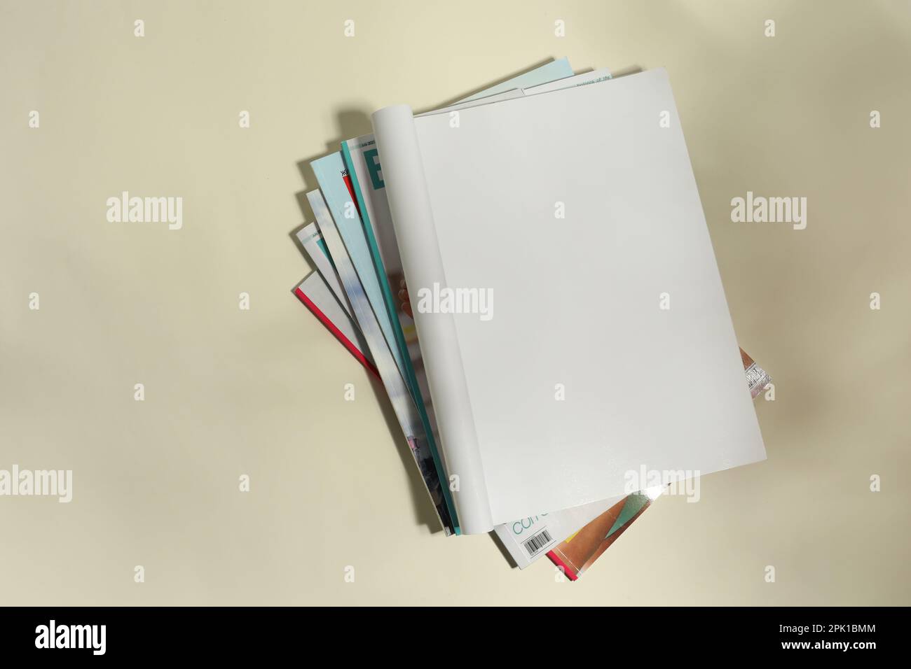 Stack of magazines and one open with blank page on beige background ...