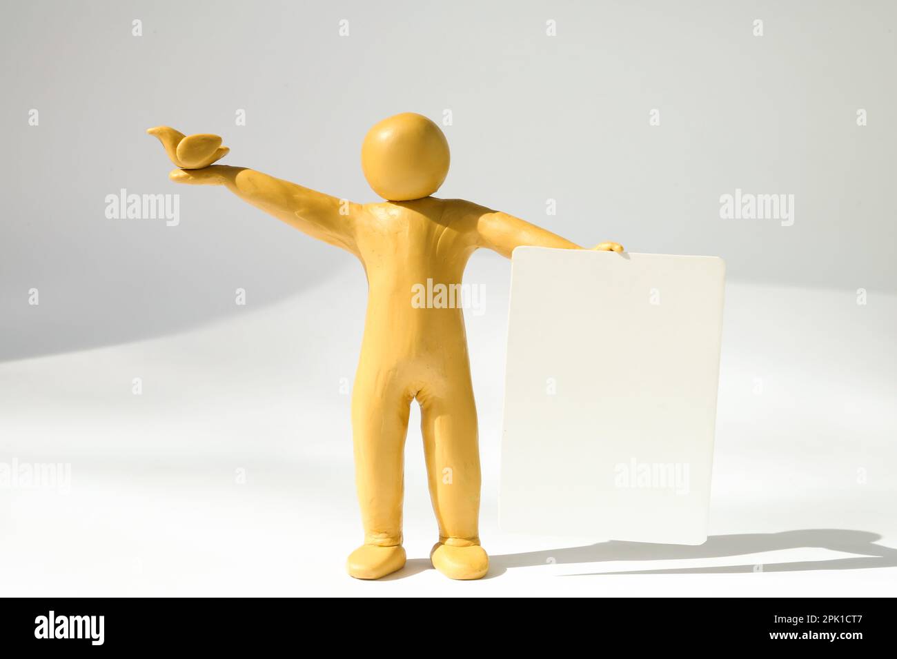 Yellow plasticine human figure with dove and blank card on white ...