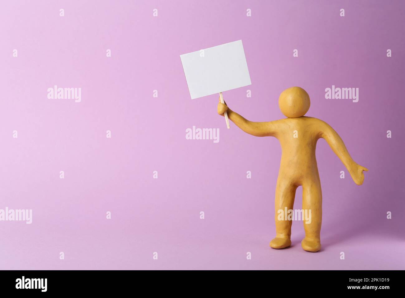Human figure made of yellow plasticine holding blank sign on violet background. Space for text ...