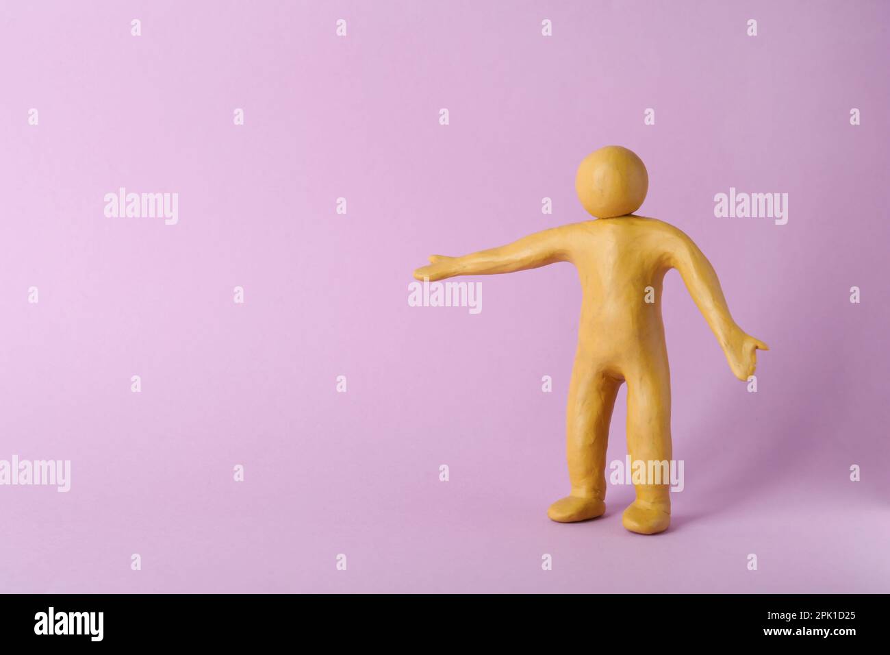 Human figure with arms wide open made of yellow plasticine on violet background. Space for text ...