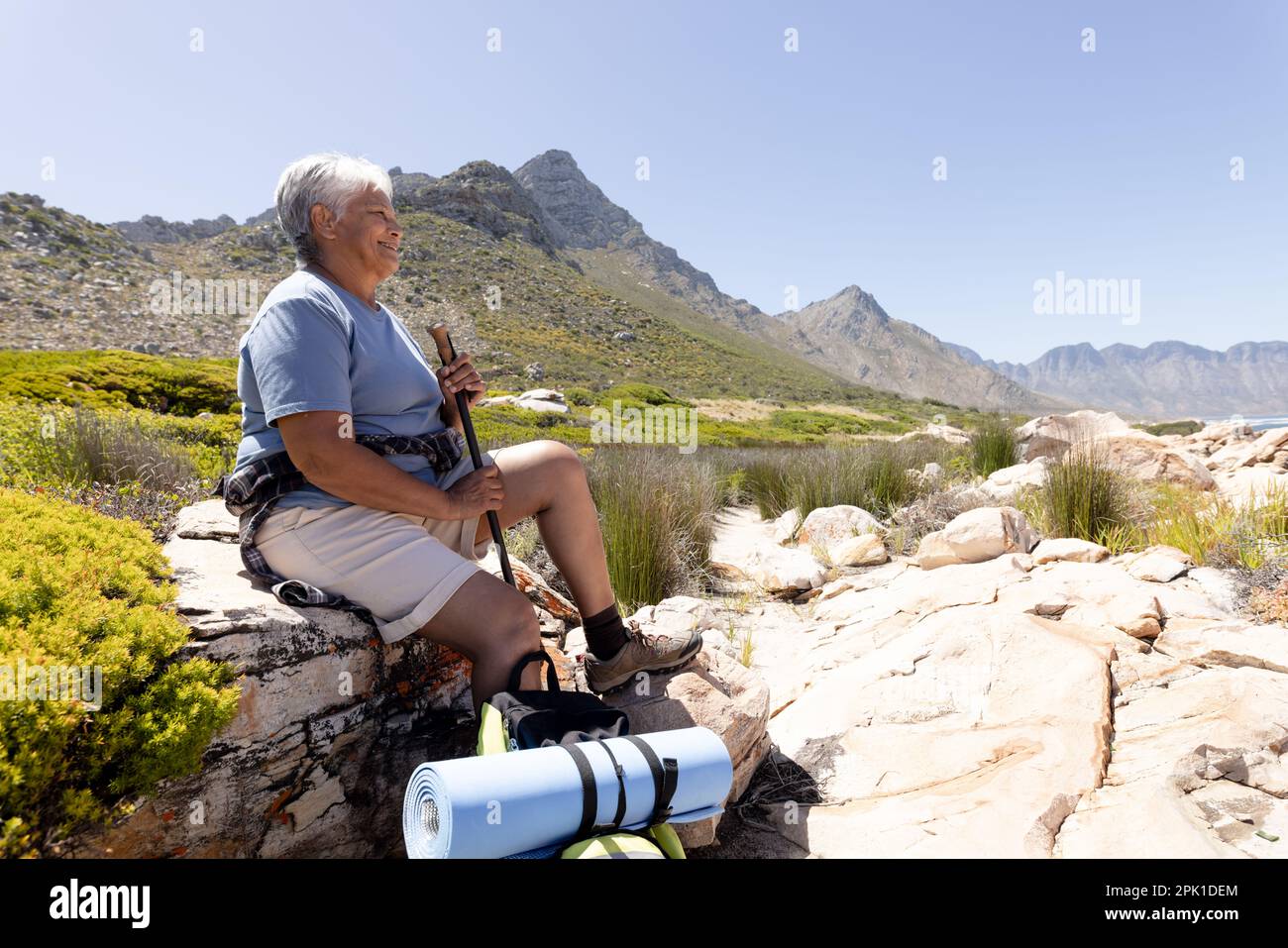 Happy senior biracial woman hiking in mountains, sitting on rock Stock ...