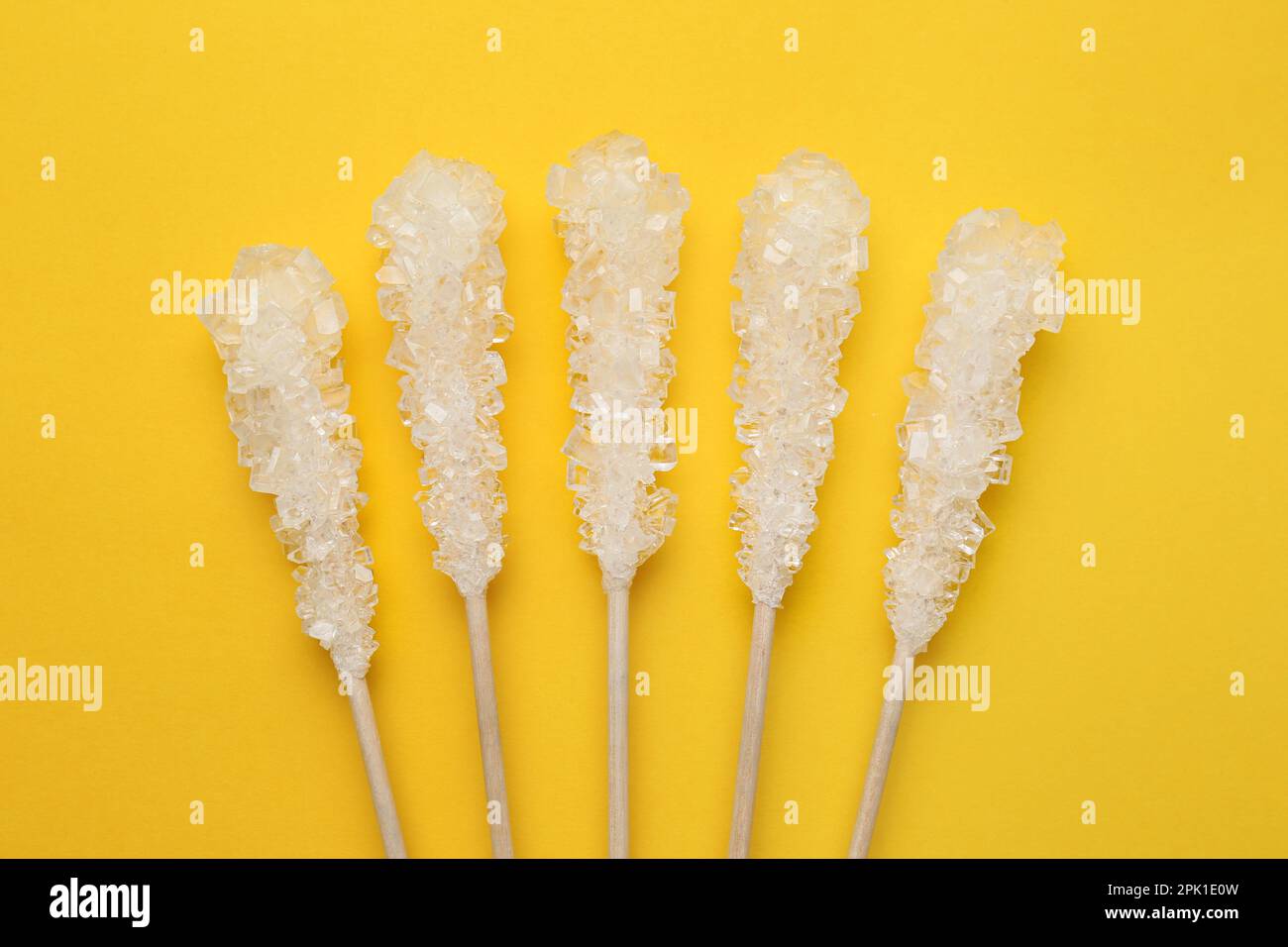 Wooden sticks with sugar crystals on yellow background, flat lay. Tasty ...