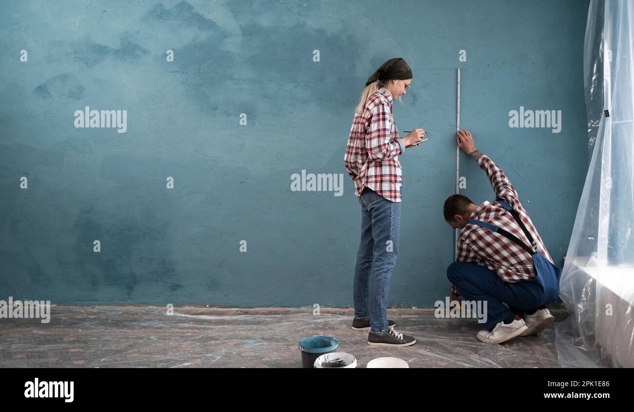 Young couple measuring wall with tape ruler, in their new house, doing ...