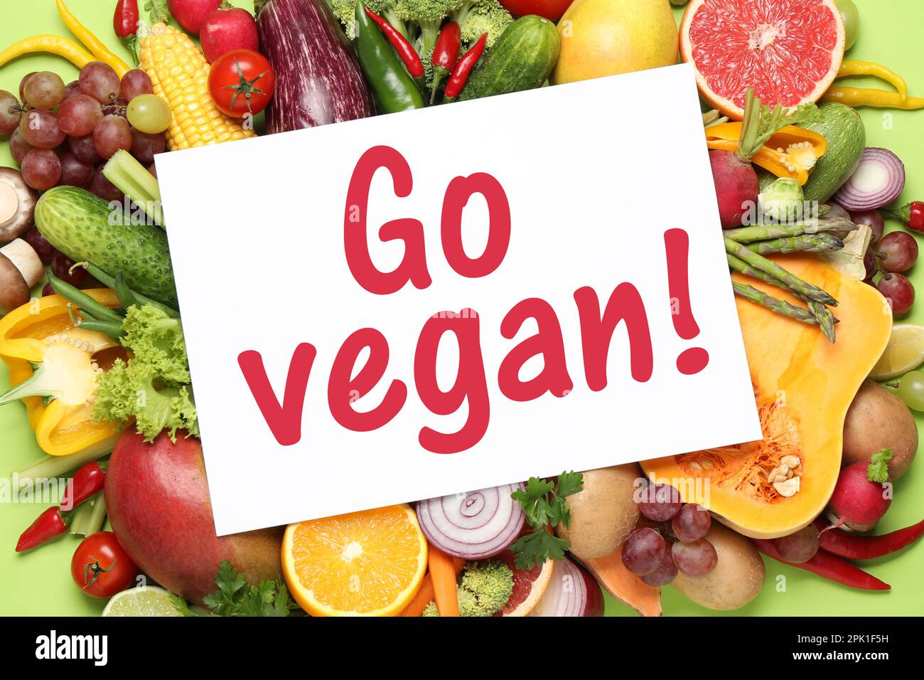 Paper card with phrase Go Vegan, fresh vegetables and fruits on green ...