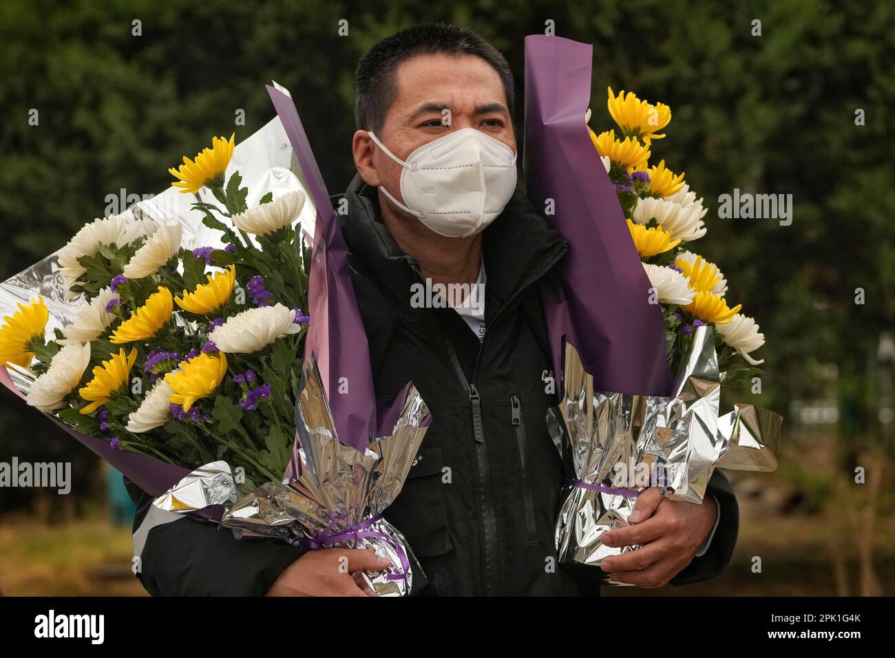 A man holding boutique of flowers walks to a cemetery during Qingming ...