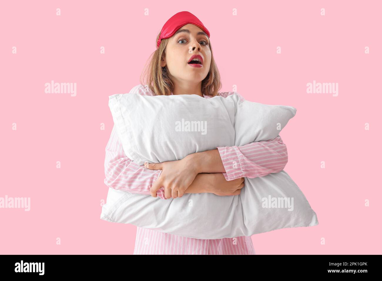 Shocked young woman in pajamas with pillow on pink background Stock ...